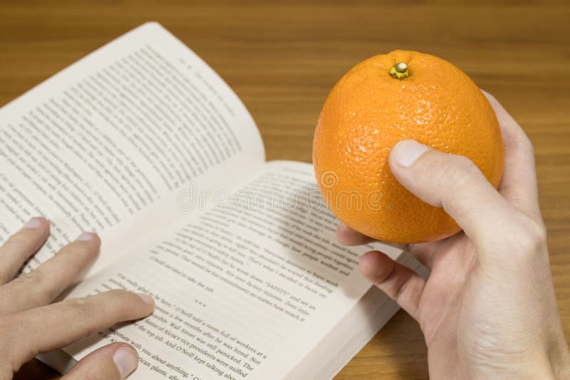 Student is Reading while is Eating an Orange on a Wood Table Stock ...