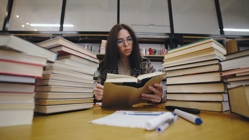 Student Reading and Taking Notes at a Desk Surrounded by a Stack of ...