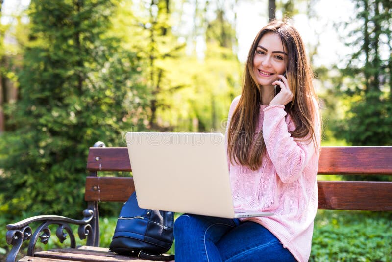 Student Sitting on a Park Bench Talking on the Phone and Working on His ...