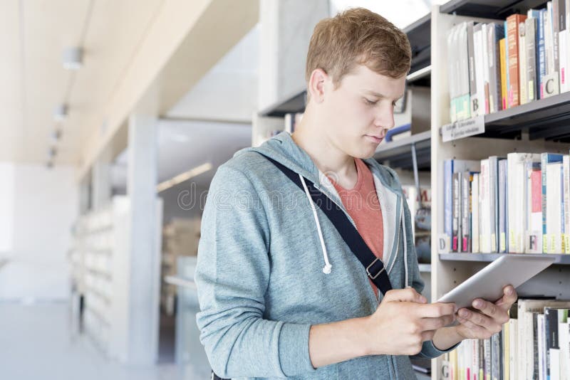 Student Using Digital Tablet while Standing by Bookshelf at Library ...