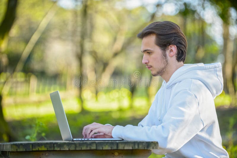 Student is Working at a Laptop in the Park. Young Guy is Typing on a ...