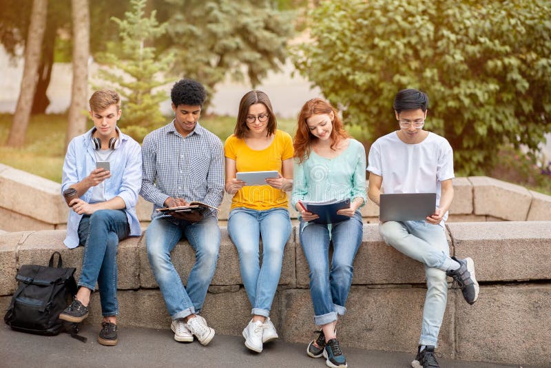 Students Learning Using Gadgets Sitting Outdoors in University Campus ...