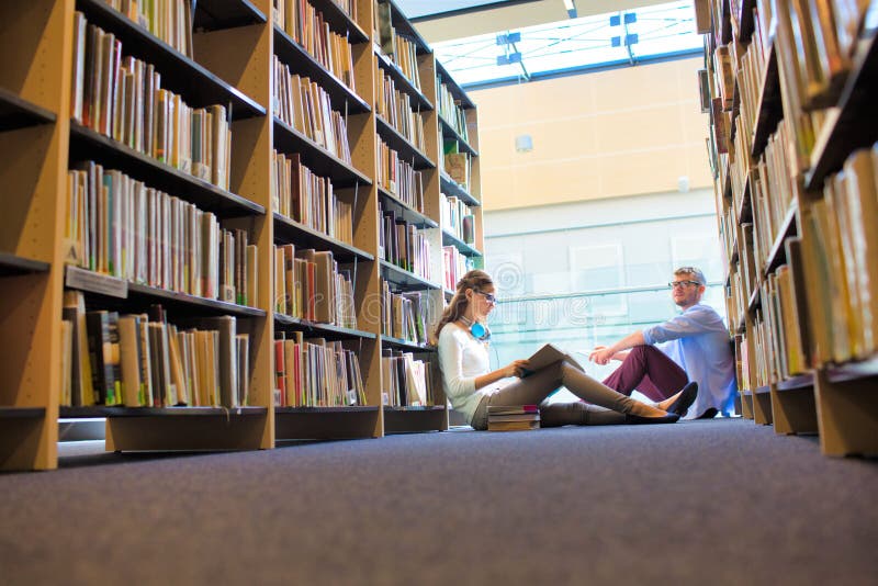 Students Reading Book while Sitting Against Bookshelf at Library Stock ...