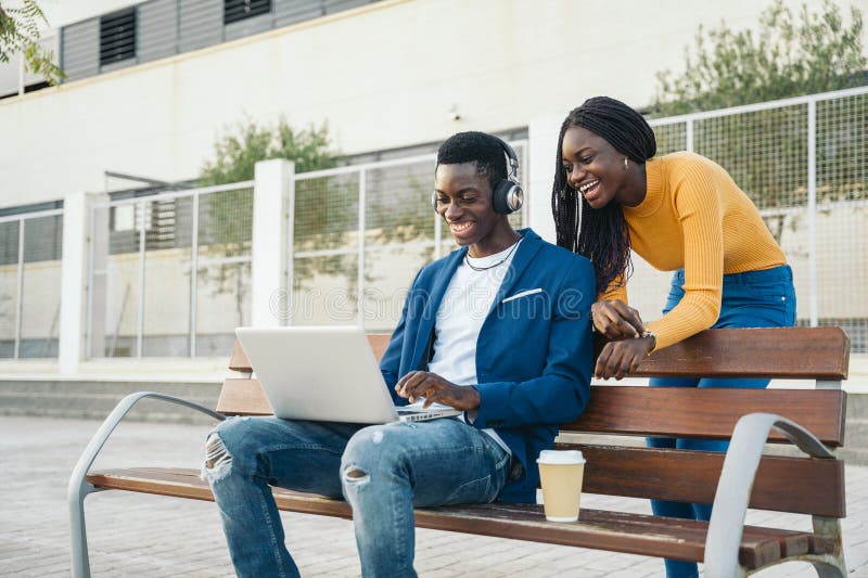 Students Working on Laptop Outdoors, Sharing Headphones and Smiling ...