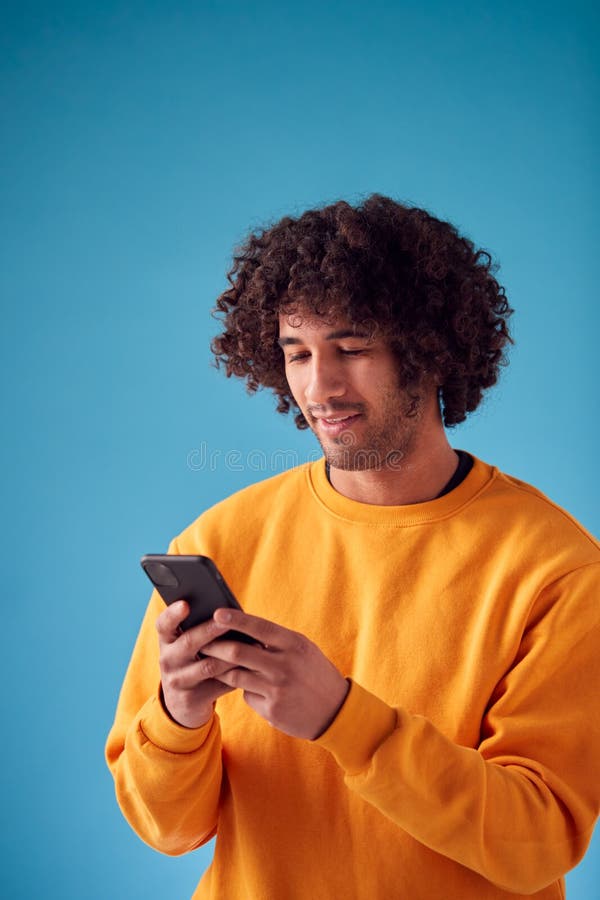 Studio Portrait of Young Man Looking at Mobile Phone Against Blue ...
