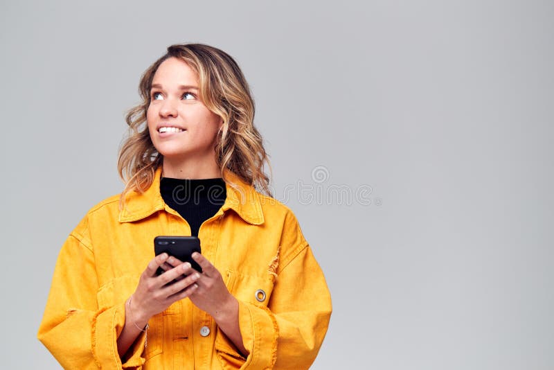 Studio Shot of Causally Dressed Young Woman Using Mobile Phone Looking ...