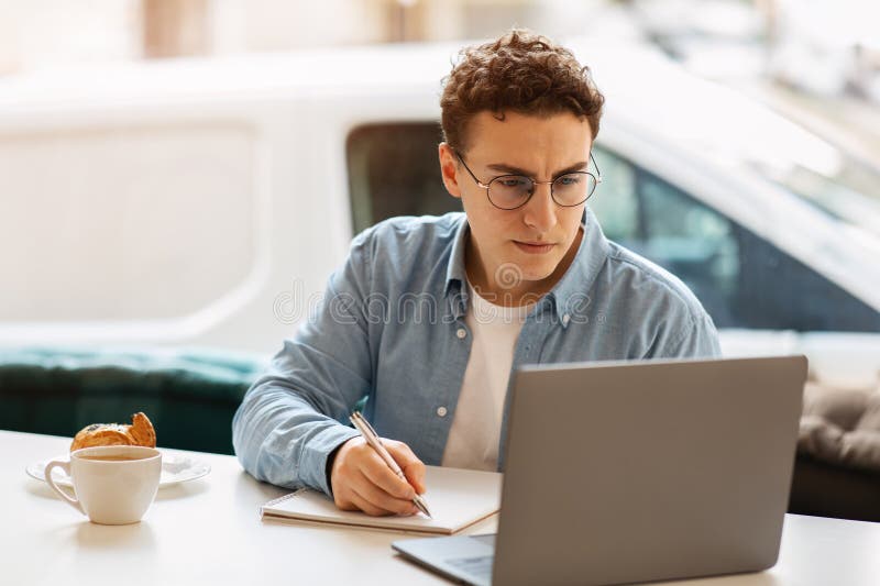 A Studious Young Man with Curly Hair and Glasses is Writing in a ...