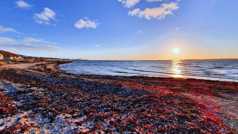 The Sun Setting Over a Beach and Ocean with Rocks in the Foreground ...