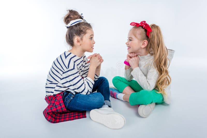 Stylish Girls Talking while Sitting on Floor on Grey Stock Photo ...