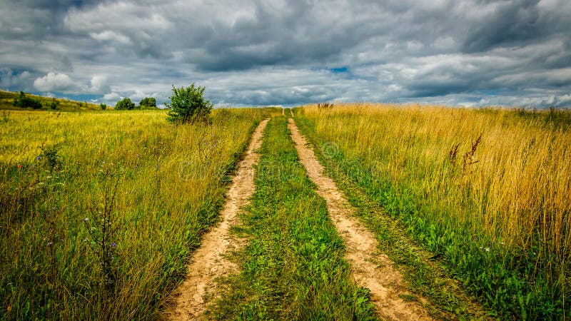 Empty Rural Dirt Road through Grassy Field Under a Cloudy Dramatic Sky ...