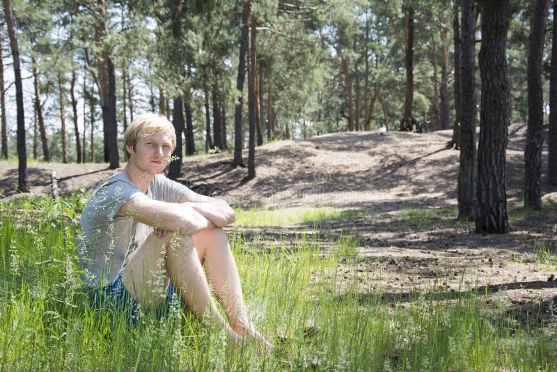 In Summer, the Pine Forest Sitting on the Grass Blond Man. Stock Photo ...