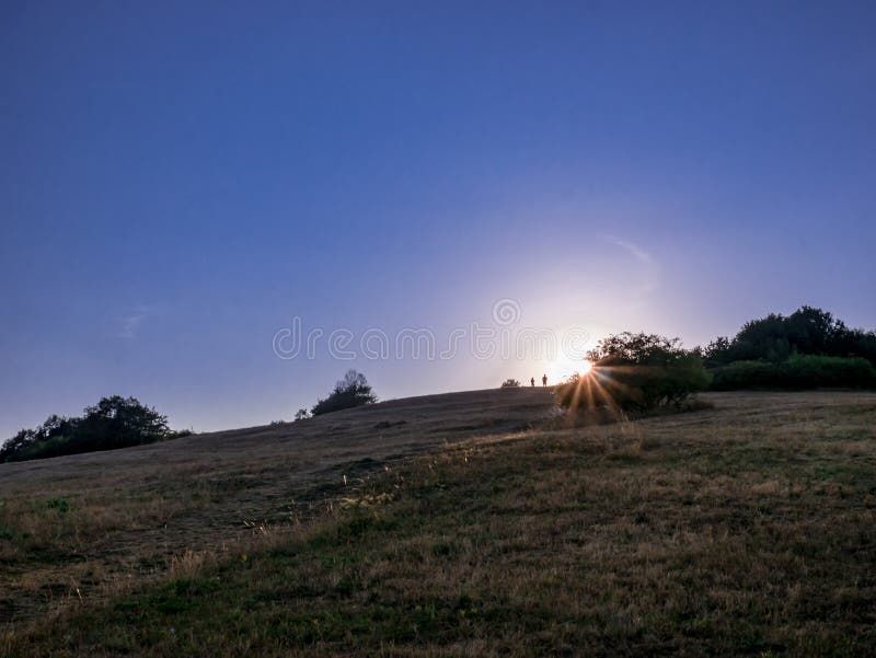 Sun Going Down Behind a Hill and on the Horizon are Two Tiny ...