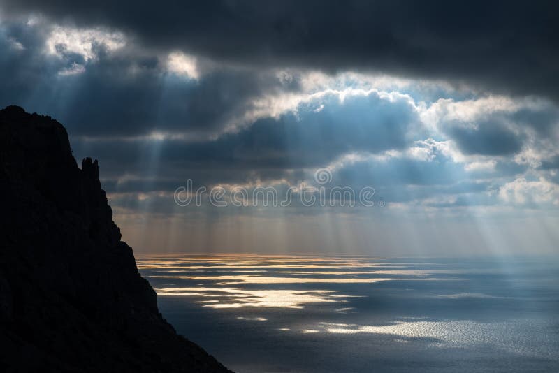 Sun Rays through Dark Clouds Over the Sea with a Reflection Stock Image ...