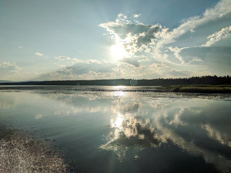 Sun Reflecting on a Calm Lake with a Distant Forest and Sky Stock Photo ...