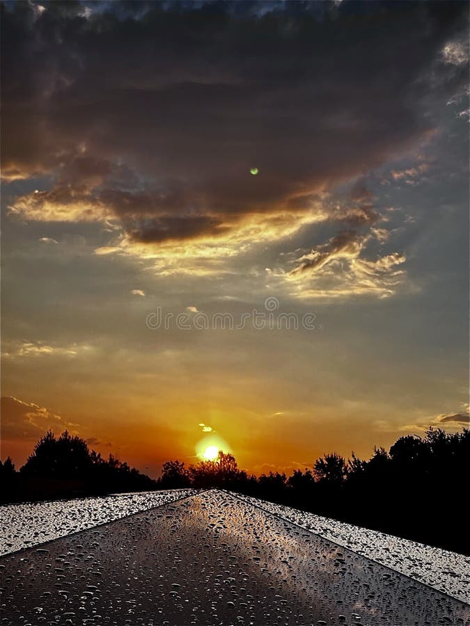 The Sun Sets Over the Water Line As it Approaches Down a Dark Road ...