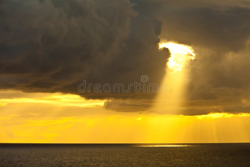 Sunbeams through Dark Clouds Over Ocean by Golden Sunrise Stock Photo ...