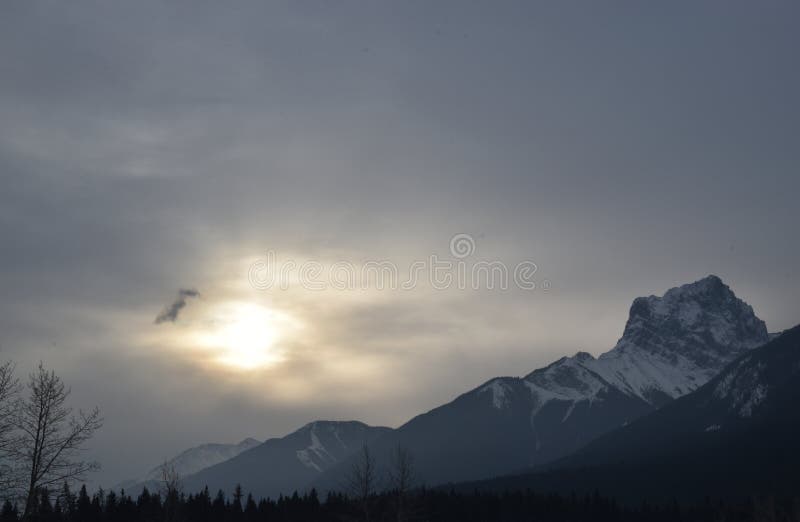 Sunlight Being Blocked by Clouds Over Snowy Mountain Peaks Stock Photo ...