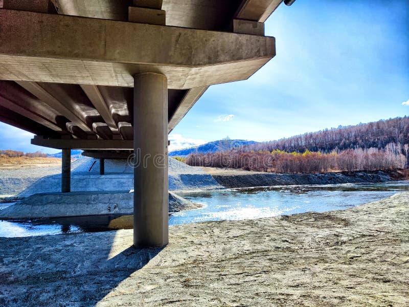 Underneath a Bridge by the Riverbank with Mountains in the Background ...