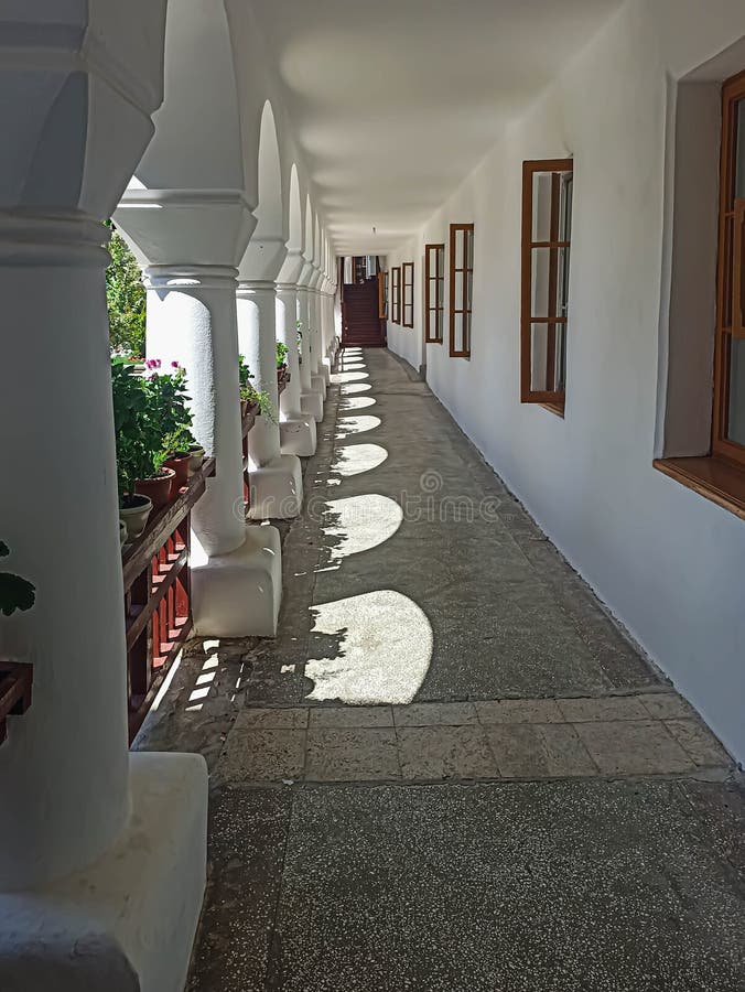 Sunlit Corridor with Arches and Wooden Windows in a Serene Setting ...