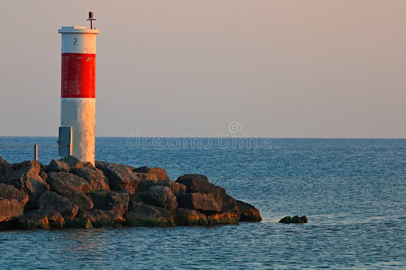 Sunrise Light Reflects Onto a Lighthouse on a Rocky Pier Stock Image ...