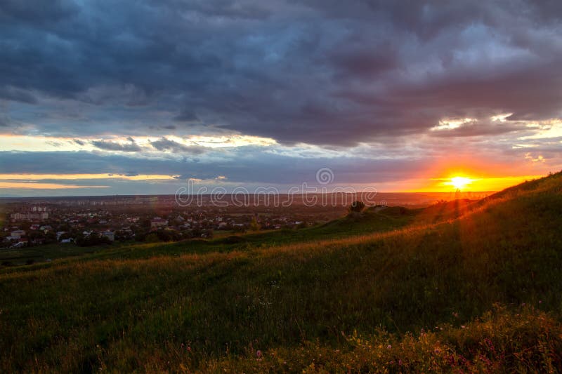 Sunset in Dramatic Cloudscape Over Wild Herb Field with Distant City in ...