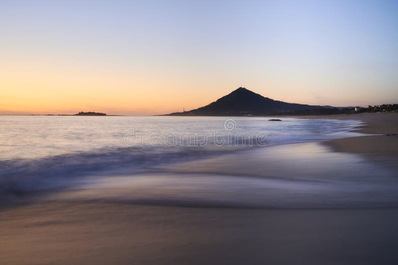 Smooth Waves Over a Sandy Beach at Sunset with Mountain in Background ...