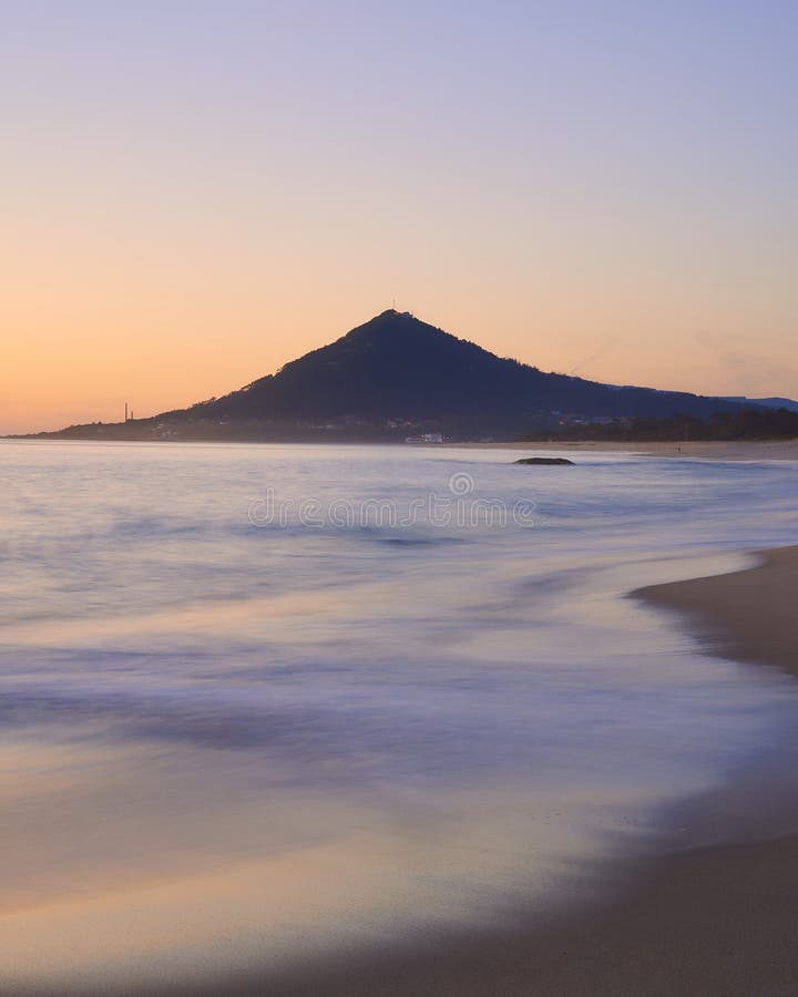Smooth Waves Over a Sandy Beach at Sunset with Mountain in Background ...