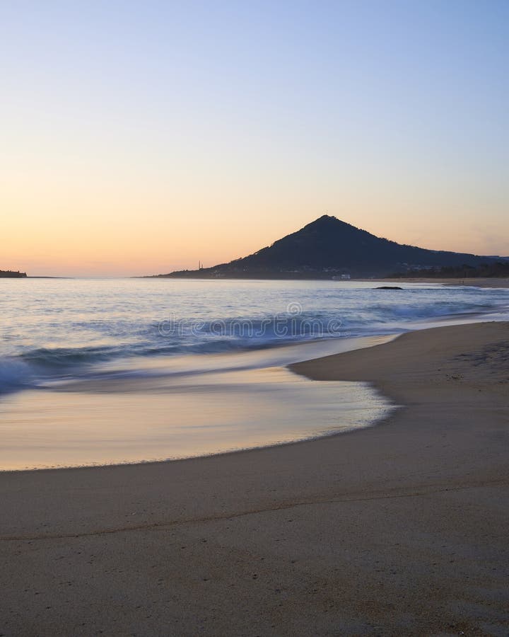 Smooth Waves Over a Sandy Beach at Sunset with Mountain in Background ...