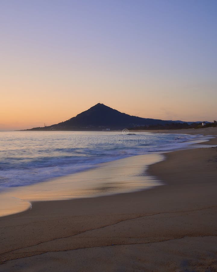 Smooth Waves Over a Sandy Beach at Sunset with Mountain in Background ...