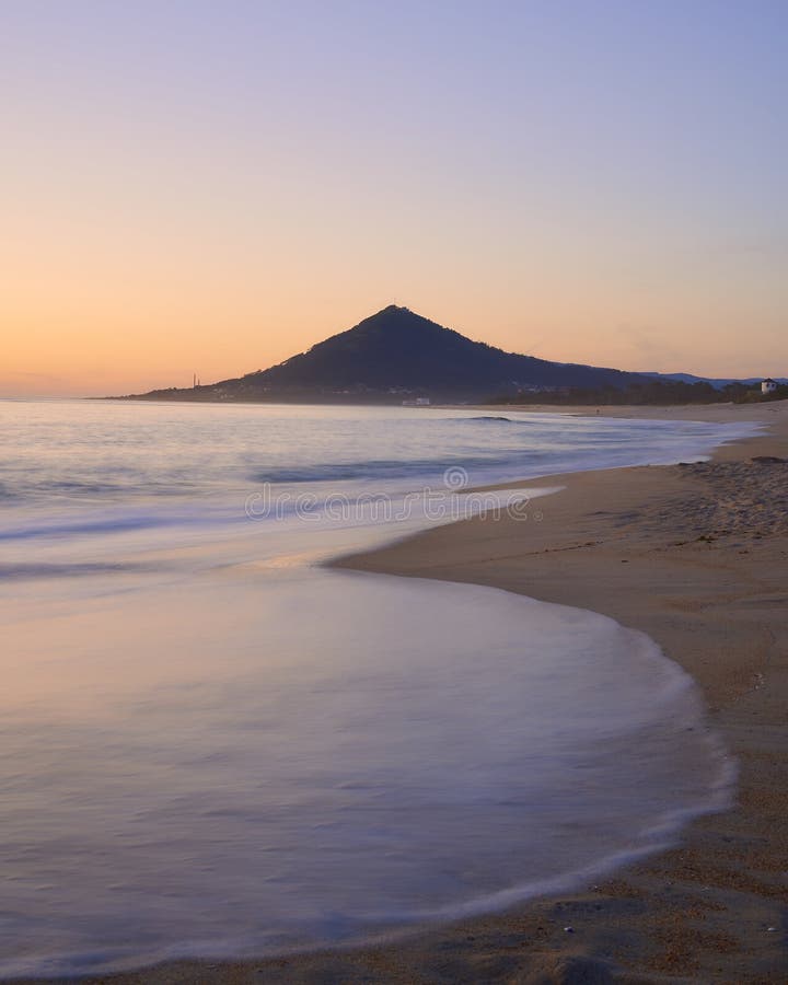 Smooth Waves Over a Sandy Beach at Sunset with Mountain in Background ...
