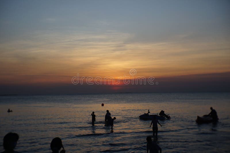 Sunset in the Ocean on a Beach with People Standing in Water Stock ...