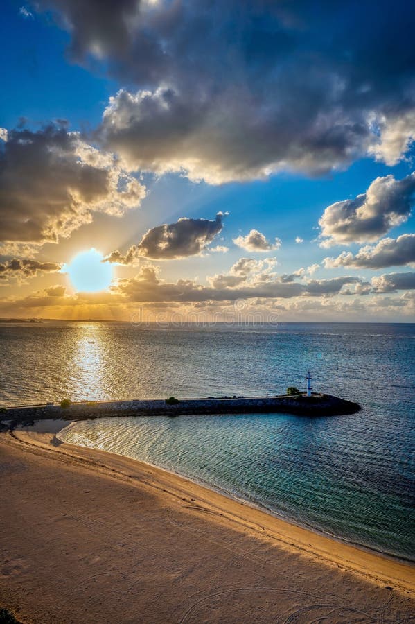 Sunset Over a Harbor Wall and Beach in Okinawa. There is a Lighthouse ...