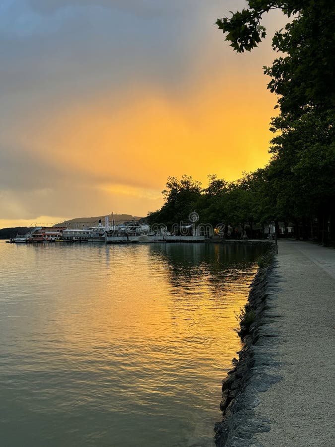 Sunset Over Waterfront with Boats and Tree-lined Path Reflecting in ...