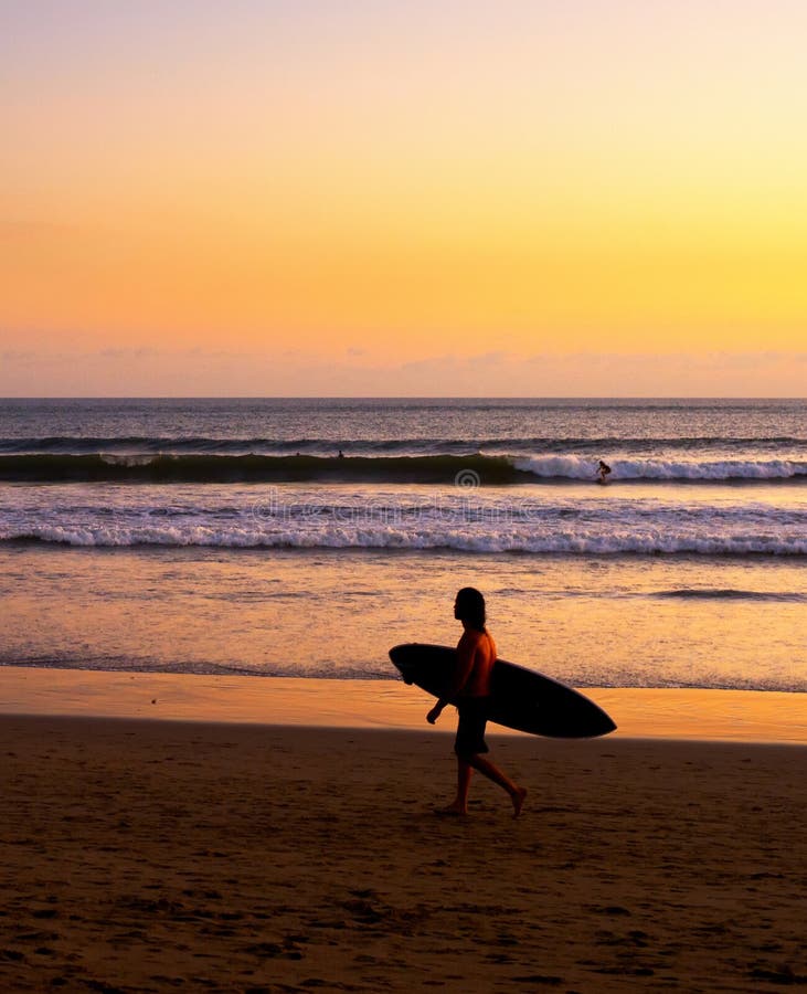 Surfer on beach at sunset stock image. Image of orange - 143648793