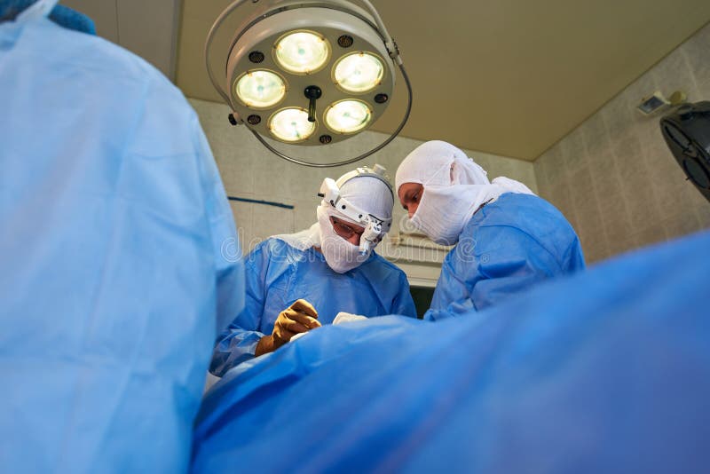 Surgery. Bottom-up View of the Faces of Surgeons Under a Round Surgical ...