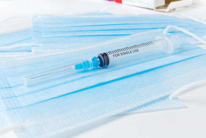 Syringe with a Needle Cap on a Blue Protective Mask Stock Photo - Image ...