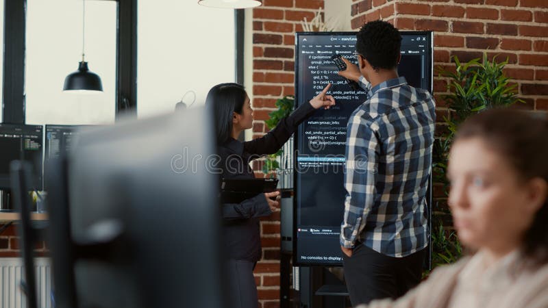 System Developers Analyzing Code On Wall Screen Tv Looking For Errors Comparing Results On