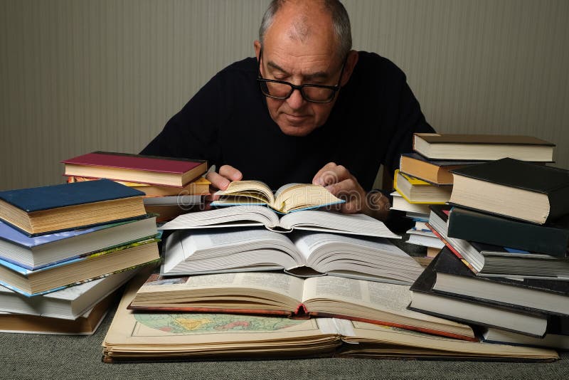 An Elderly Man Reading a Book at a Table Heaped with Books Stock Image ...