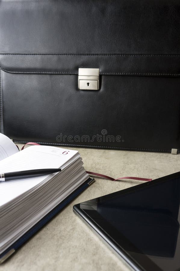 On the Table is an Open Notepad with a Pen, a Tablet and a Briefcase ...