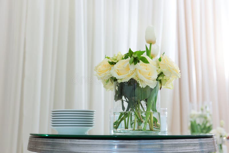 On the Table There is a Vase with White Roses and a Stack of Plates ...