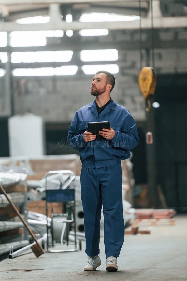 With Tablet in Hands. Factory Worker in Blue Uniform is Indoors Stock ...