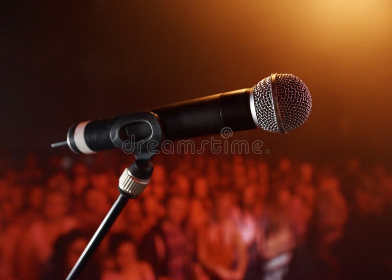 Take the stage.... A microphone standing on a stage with a crowd in the ...