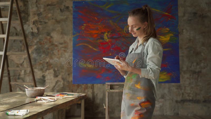 A Talented Artist Using a Tablet on the Background of a Painted Picture ...