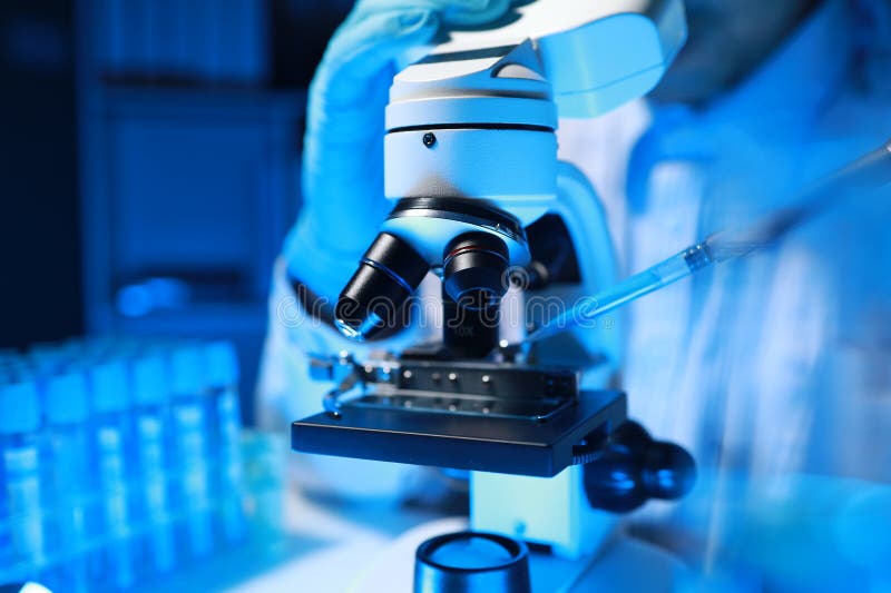 A Talented Scientist Sits in His Lab while Using a Microscope To Look ...