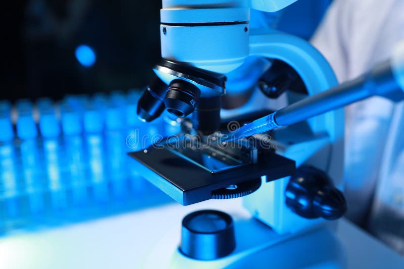 A Talented Scientist Sits in His Lab while Using a Microscope To Look ...