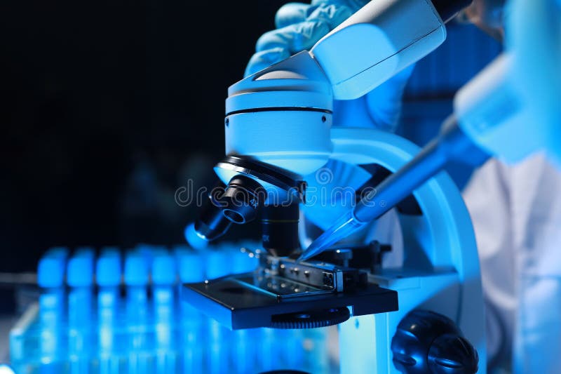 A Talented Scientist Sits in His Lab while Using a Microscope To Look ...