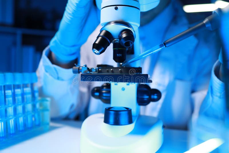 A Talented Scientist Sits in His Lab while Using a Microscope To Look ...