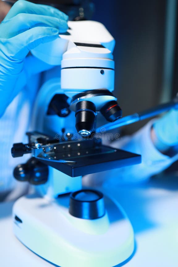 A Talented Scientist Sits in His Lab while Using a Microscope To Look ...