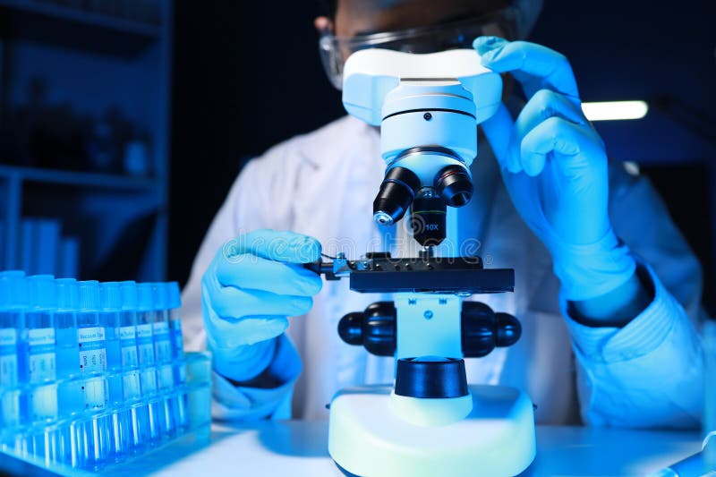 A Talented Scientist Sits in His Lab while Using a Microscope To Look ...