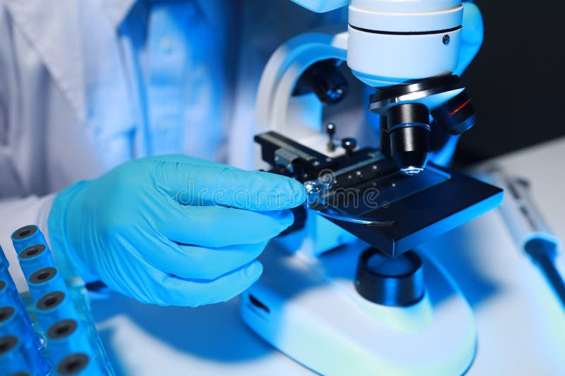 A Talented Scientist Sits in His Lab while Using a Microscope To Look ...